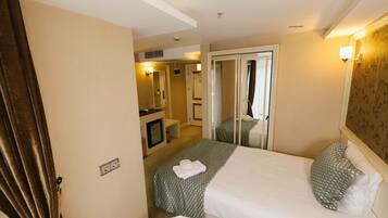 Quarto de hotel com cama, espelho, cômoda e banheiro visível através de uma porta aberta.