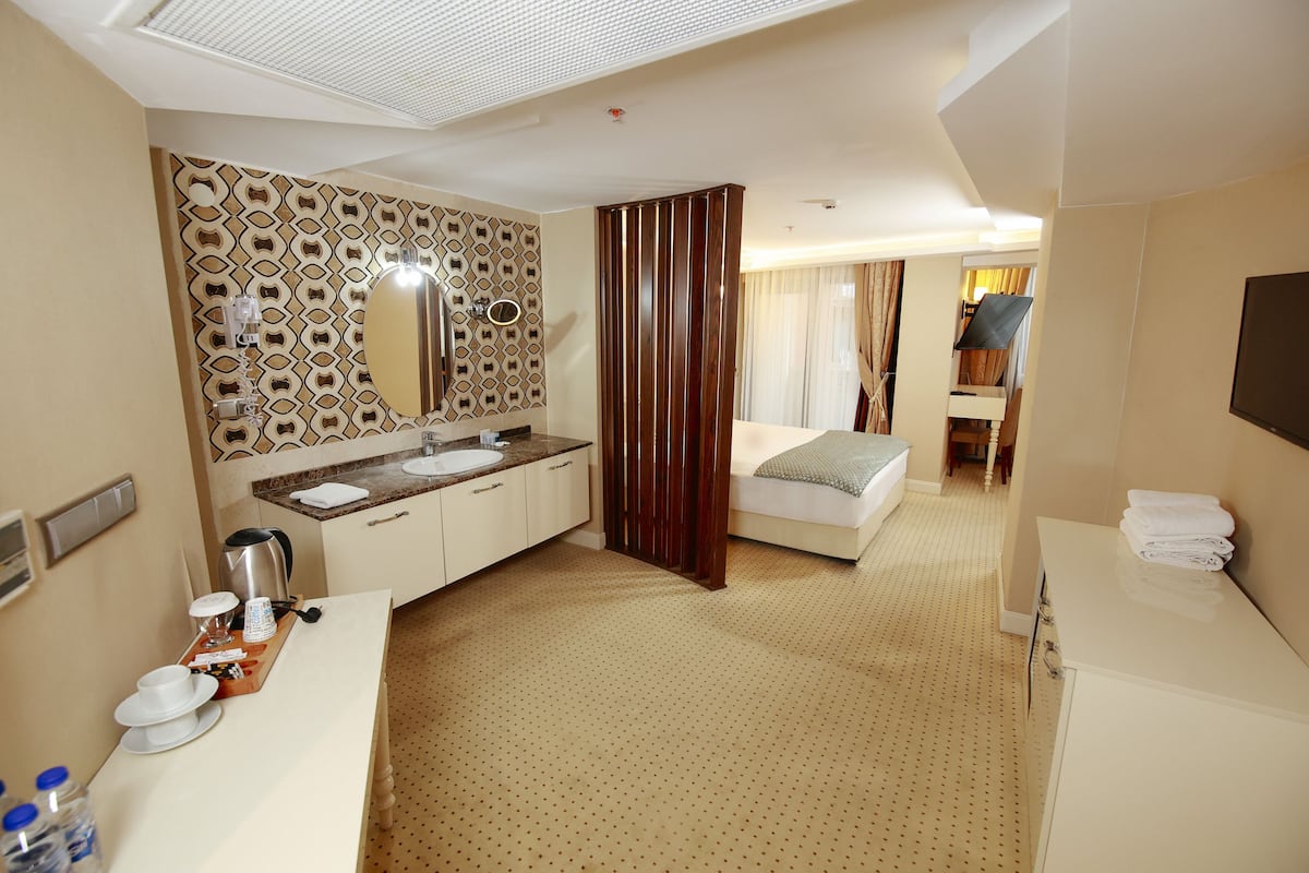 Quarto de hotel com banheiro, cama, escrivaninha e televisão.
