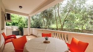 Mesa redonda com toalha branca e cadeiras laranja numa varanda com vista para árvores e um muro de pedra.