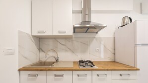 Uma cozinha moderna com armários brancos, painel de fundo de mármore, exaustor de aço inoxidável, bancada de madeira e fogão a gás embutido.