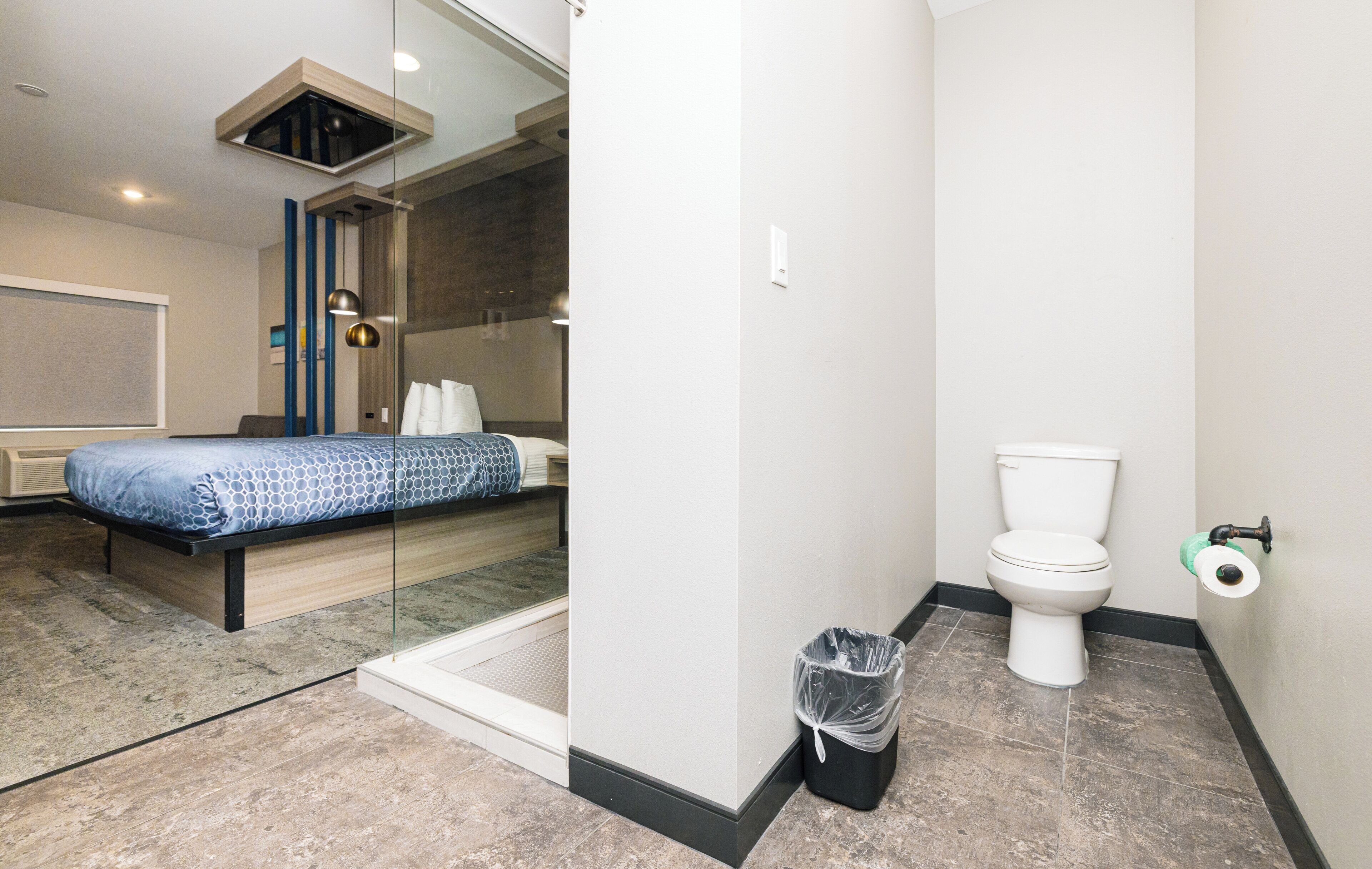 Quarto de hotel com cama, mesa de cabeceira e banheiro com vaso sanitário e chuveiro.