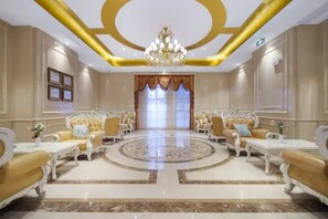 Um hall de hotel luxuoso, com lustres elaborados, assentos confortáveis e uma entrada imponente.