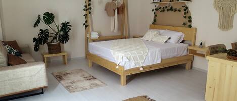 Um quarto com cama de madeira, mesa de cabeceira, planta pendente e um painel de macramé na parede.