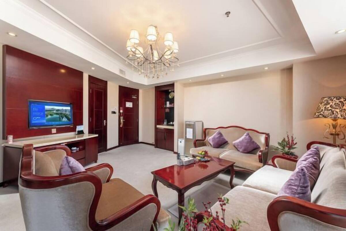 Um saguão de hotel com televisão, um candelabro, um balcão de recepção e áreas de estar.