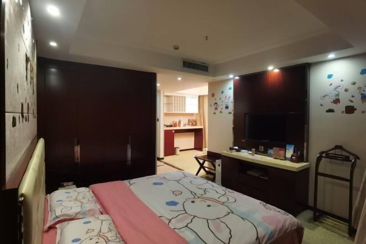 Quarto de hotel com cama, escrivaninha, televisão e guarda-roupa.