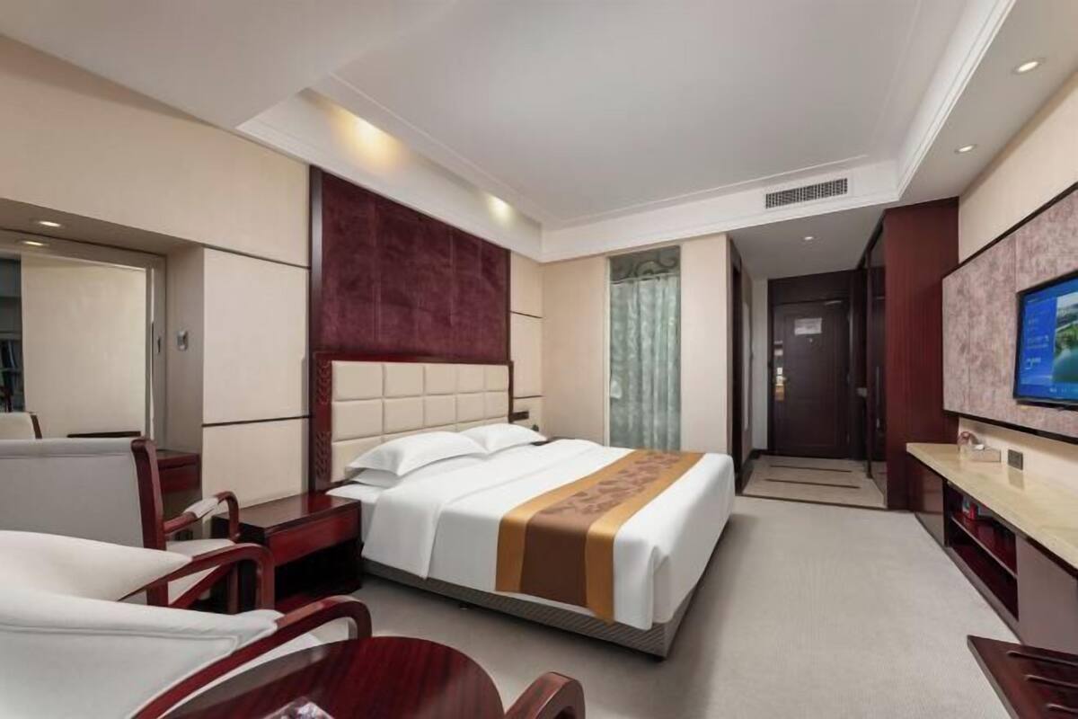 Quarto de hotel com uma cama grande, uma mesa, uma cadeira, uma TV e um banheiro visível através de uma porta aberta.