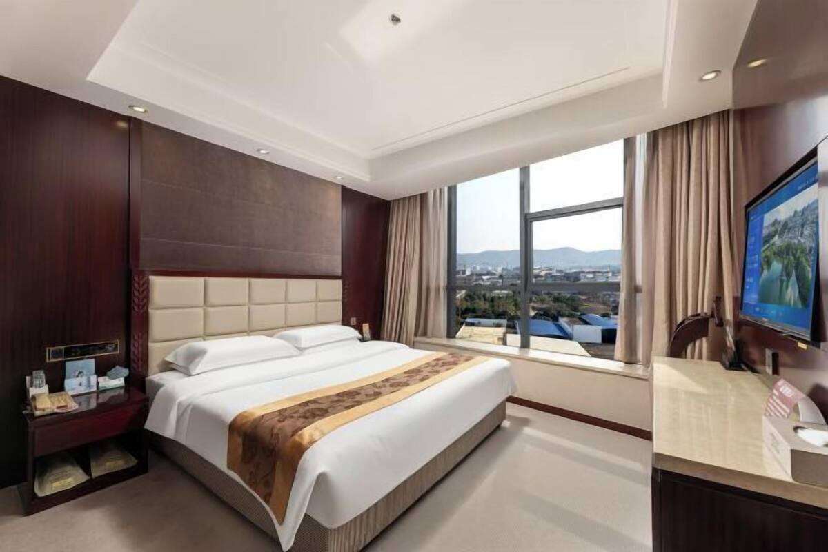 Quarto de hotel com uma cama grande, uma mesa de trabalho e vista para a cidade pela janela.