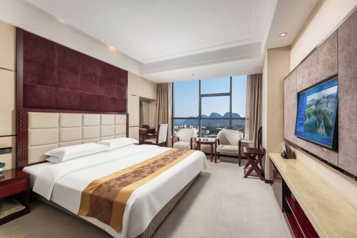 Quarto de hotel com uma cama grande, uma escrivaninha, uma cadeira e uma televisão.