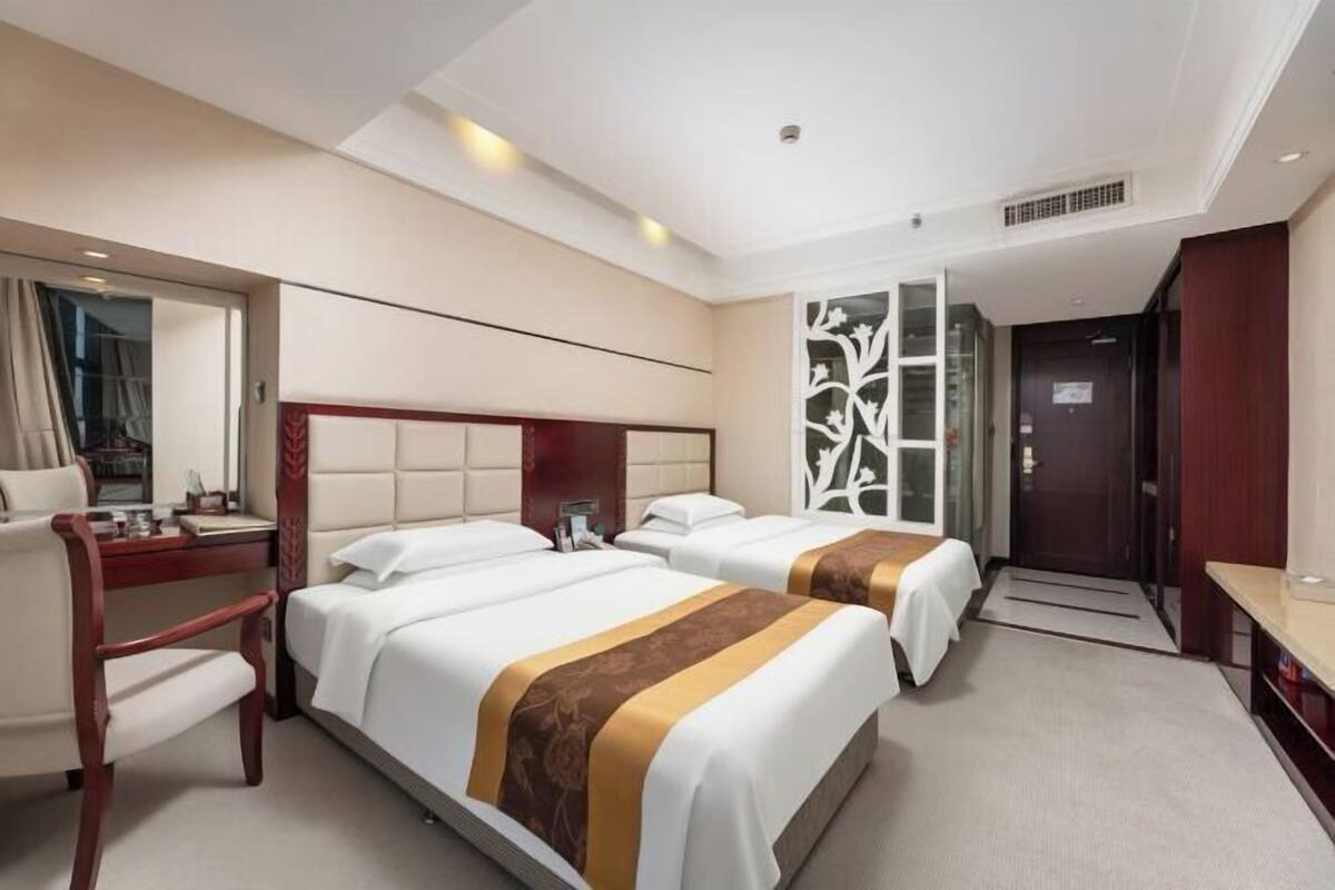 Quarto de hotel com duas camas, uma escrivaninha, uma cadeira e um guarda-roupa.