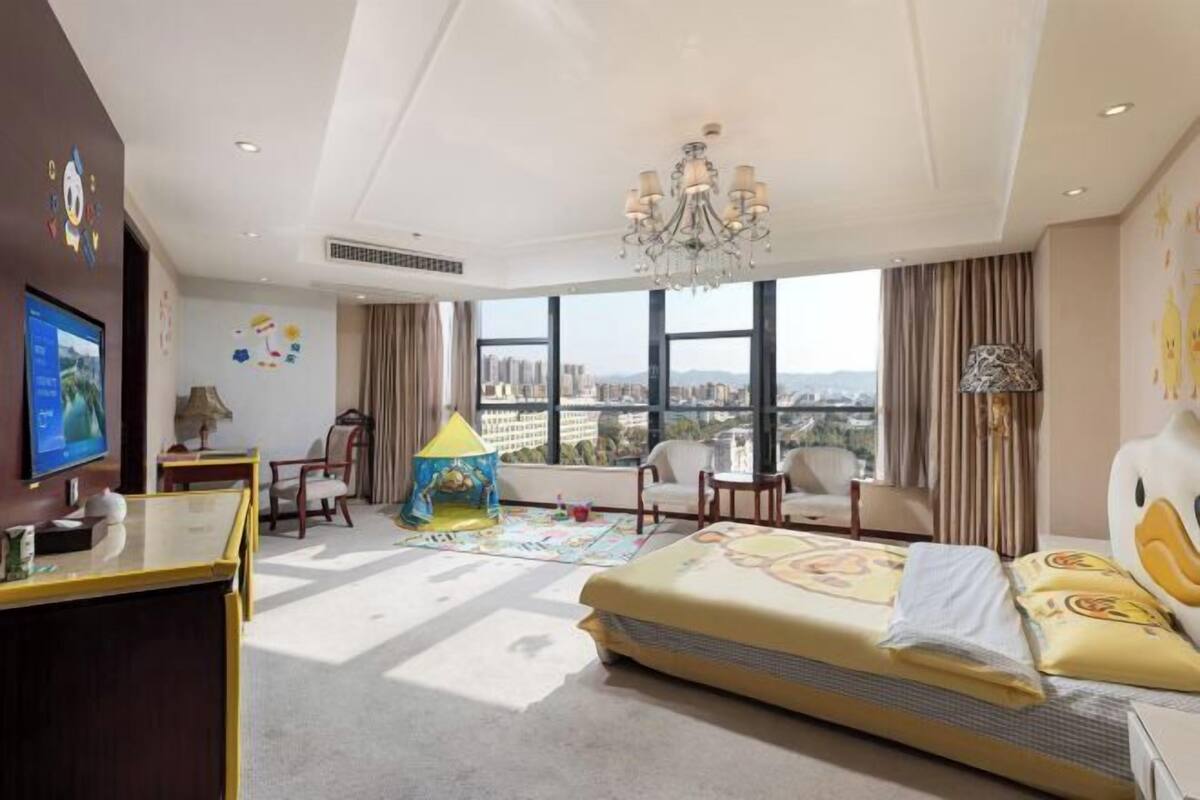 Quarto de hotel com uma cama grande, uma escrivaninha, uma cadeira, uma mesinha e uma janela com vista para a cidade.