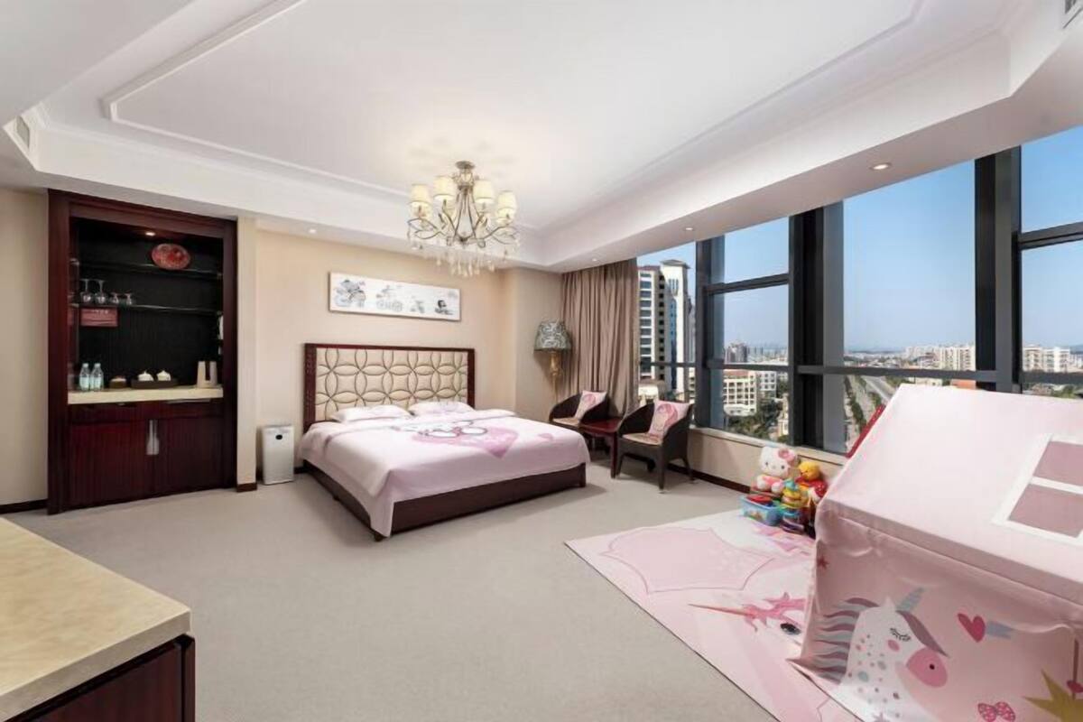 Quarto de hotel moderno com uma cama grande, uma toucador, um candelabro e vista da cidade através de amplas janelas.