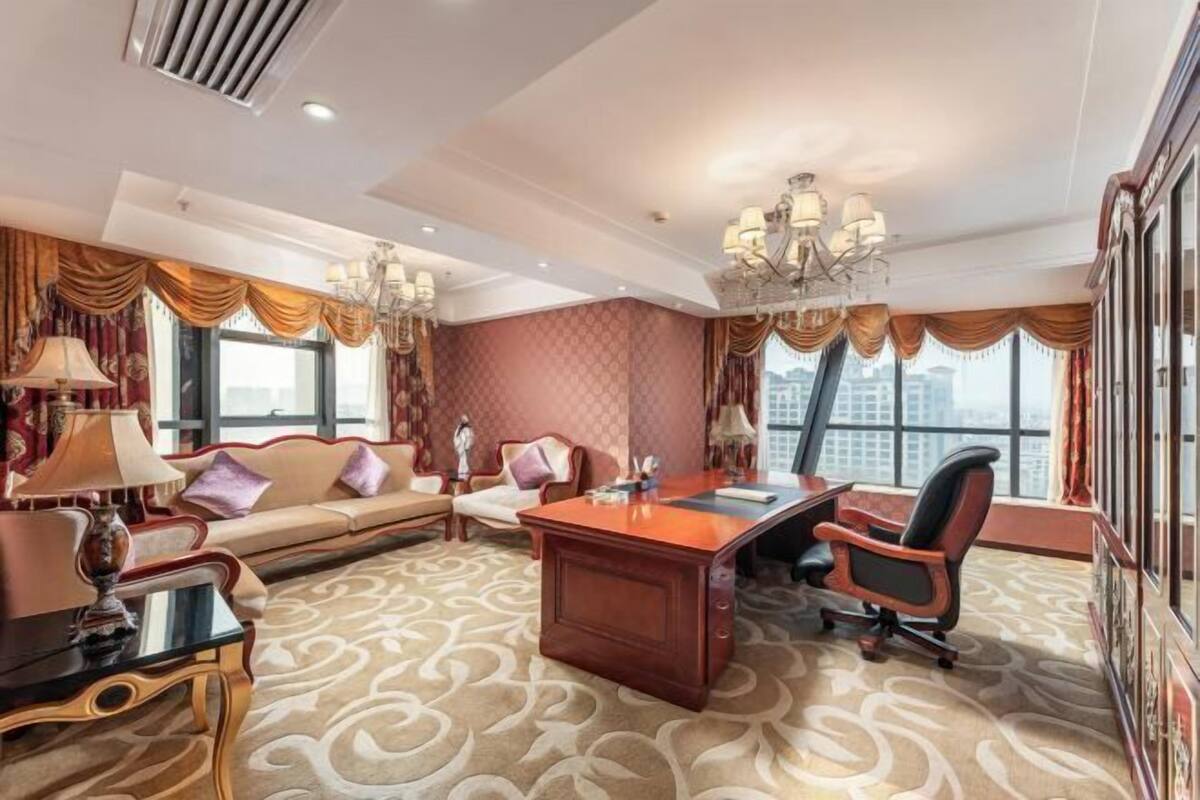 Um quarto espaçoso com uma escrivaninha grande, um sofá e um lustre.