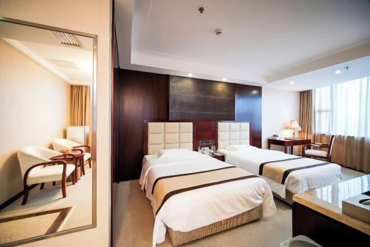 Quarto de hotel com duas camas, área de estar com uma poltrona e uma mesinha, e um espelho grande.