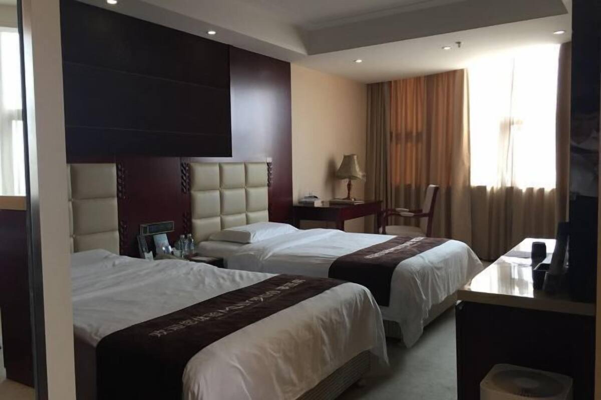 Quarto de hotel com duas camas, uma mesa, uma cadeira, uma mesinha de cabeceira e uma televisão.