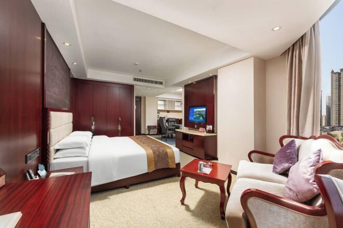 Quarto de hotel com cama, escrivaninha, cadeira e televisão.