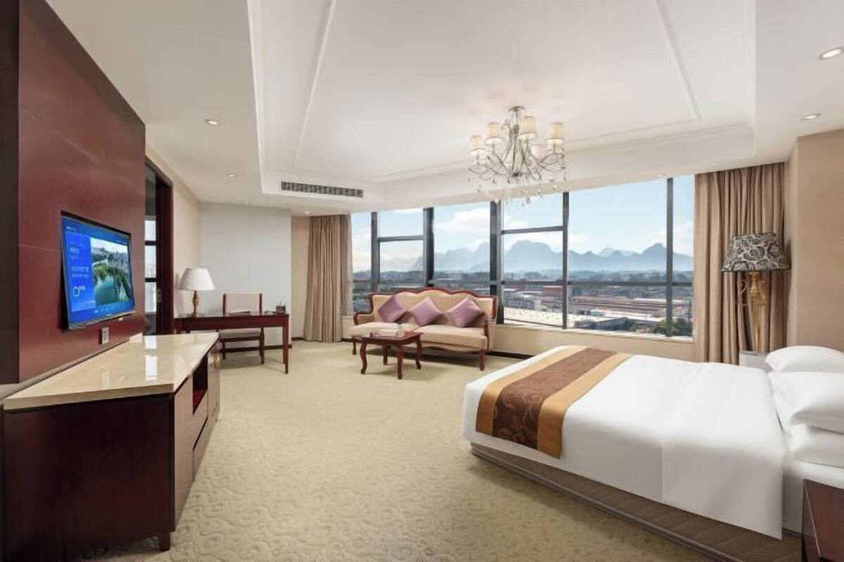 Quarto de hotel com uma cama grande, escrivaninha, sofá e televisão.