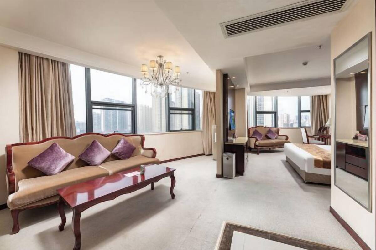 Quarto de hotel com sofá, cama, escrivaninha e uma grande janela com vista para a cidade.