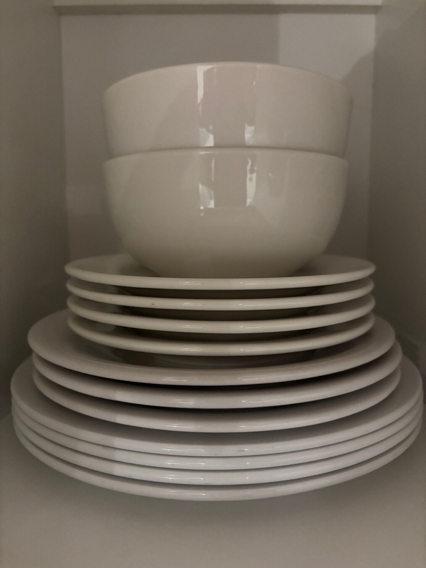 Uma pilha de pratos e tigelas brancas dentro de um armário.