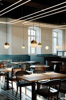 Interior de restaurante moderno, com pé-direito alto, iluminação pendente e uma combinação de mesas e cadeiras de madeira e estofadas.