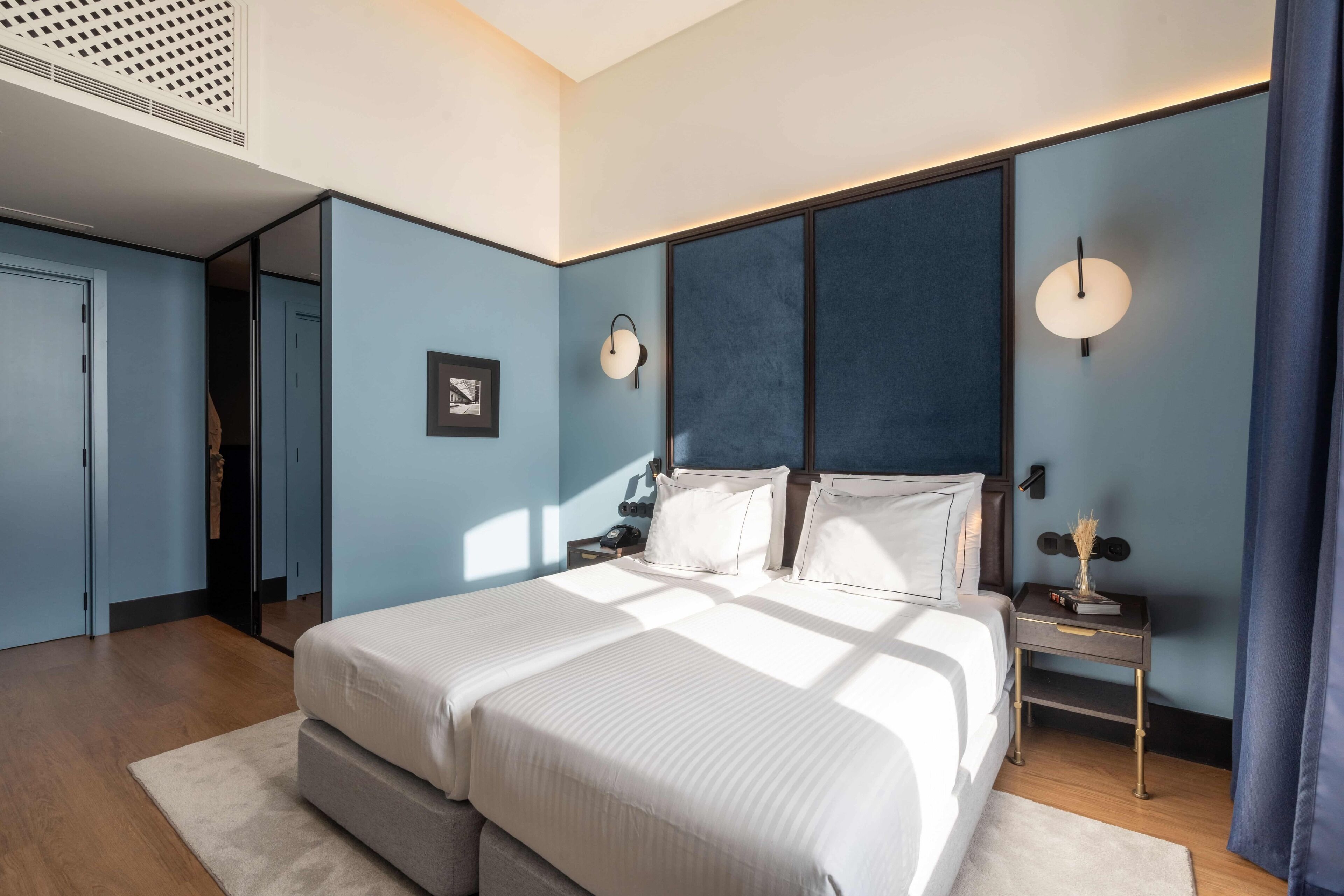 Quarto moderno com uma cama grande, uma mesa de cabeceira e uma luminária na parede.