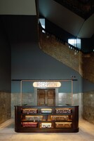 Uma área de recepção com uma placa identificada como “RECEPTION” sobre uma porta de madeira, rodeada por uma exposição de malas.