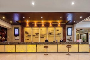 Uma área de recepção de hotel com balcão de mármore, teto de madeira e uma tela digital.