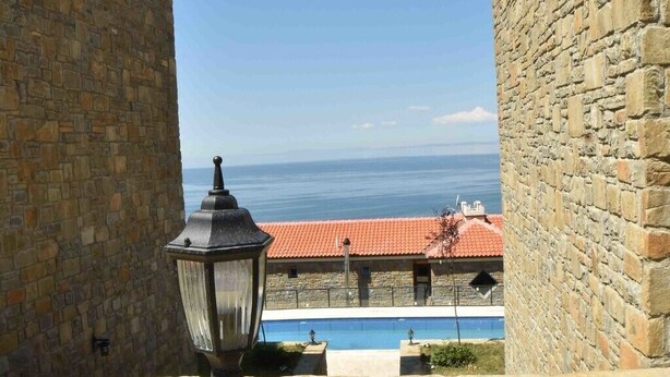 Um edifício de pedra com vista para o mar e uma estrutura de telhado vermelho ao fundo.
