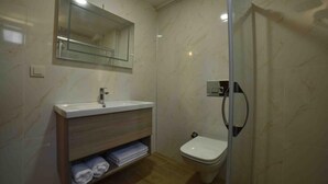 Um banheiro moderno com parede de mármore, box de vidro, pia branca e vaso sanitário.