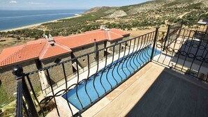 Uma varanda com piscina, com vista para uma praia e paisagem montanhosa.