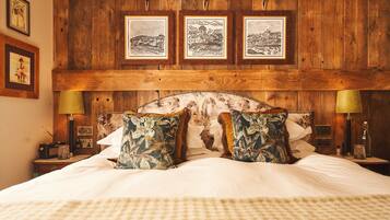 Quarto com cabeceira de madeira, cama com roupa de cama branca, duas mesas de cabeceira com abajures e três quadros na parede.