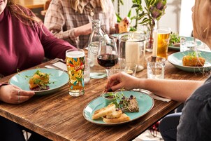 Uma mesa de madeira com pratos de comida, copos de cerveja e uma garrafa de cerveja.