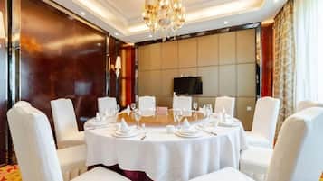 Uma sala de conferências com uma mesa redonda, cadeiras brancas e um candelabro.