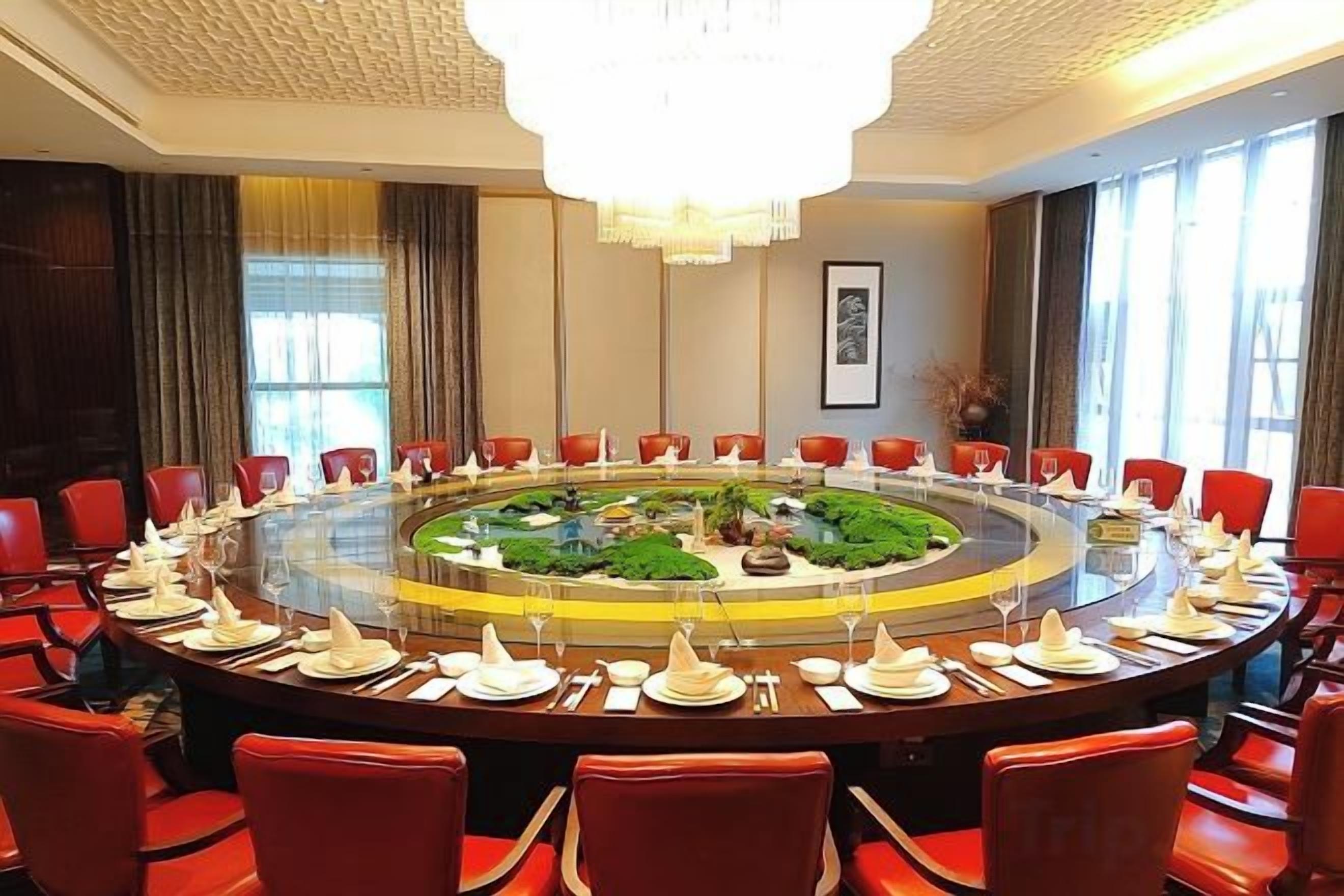 Sala de conferências com mesa redonda, cadeiras vermelhas e um lustre.