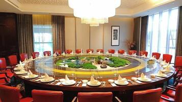Sala de conferências com mesa redonda, cadeiras vermelhas e um lustre.
