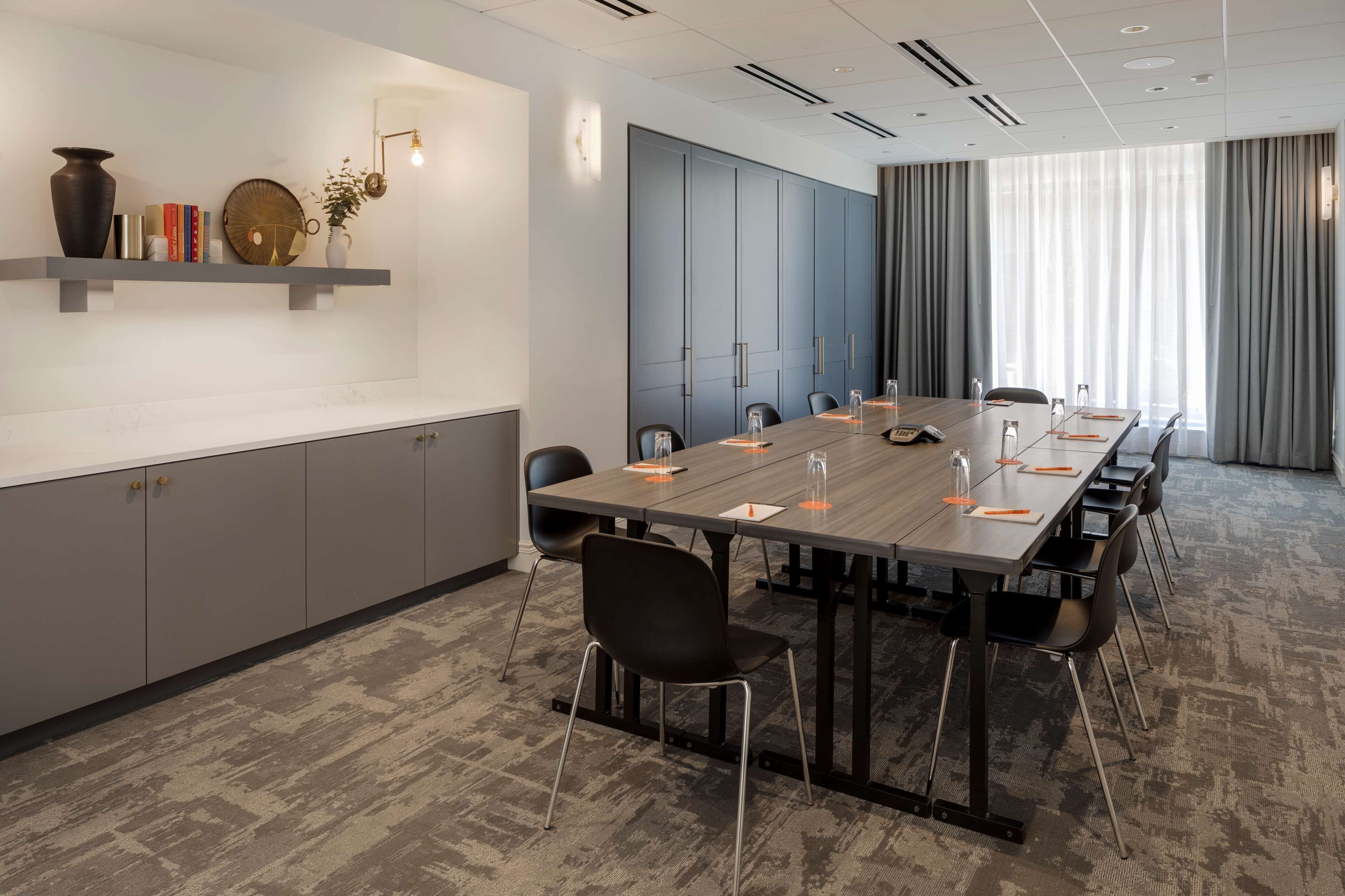 Uma sala de conferências com uma mesa comprida, cadeiras e uma estante com livros e objetos decorativos.