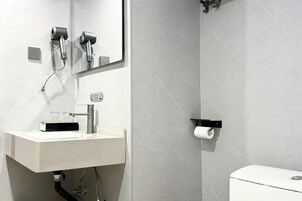 Uma casa de banho moderna com uma pia branca, um espelho, um secador de cabelo e uma sanita.