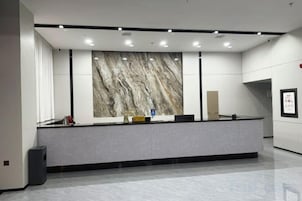 Uma área de recepção com parede de mármore, balcão de atendimento e lixeira.