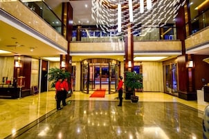 Um hall de hotel com carpete vermelho, balcão de recepção e uma grande estrutura decorativa no teto.