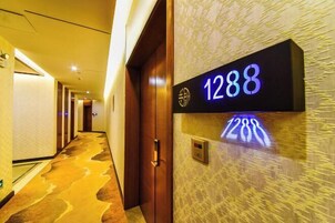 Um corredor de hotel com piso carpete, uma porta de madeira e uma placa fixada na parede com o número 1288.