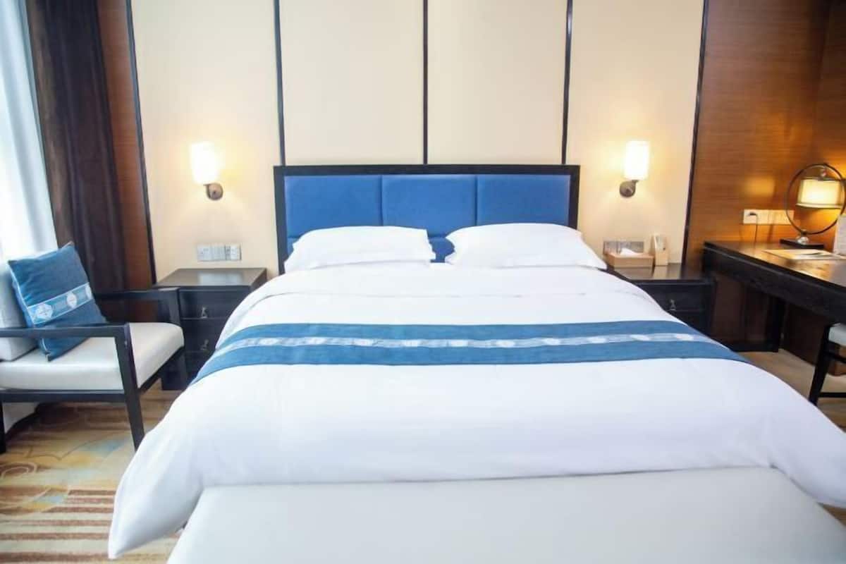 Quarto de hotel com uma cama grande, duas mesas de cabeceira, uma cadeira e um criado-mudo.