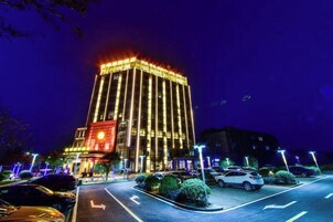Um edifício com vários andares, janelas iluminadas e um estacionamento em frente.