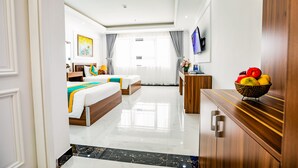 Quarto de hotel com cama, escrivaninha, televisão e uma cesta de frutas.
