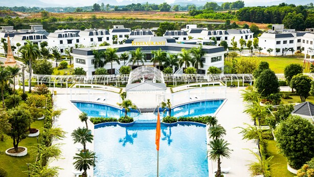 Um grande hotel com piscina, cercado por vegetação e palmeiras.