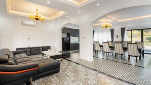 Uma sala ampla com um sofá moderno, mesa de jantar com cadeiras e cozinha ao fundo.