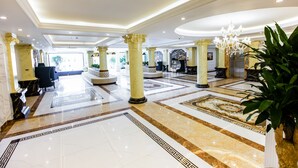 Um hall amplo com piso de mármore, colunas e um lustre.