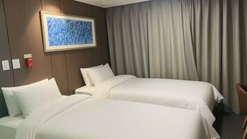 Quarto de hotel com duas camas, uma janela grande com cortinas, um quadro na parede e uma cadeira.