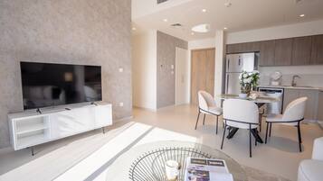 Uma sala de estar moderna com uma TV de tela plana, uma mesa de centro de vidro e um espaço de jantar com cadeiras e uma mesa.