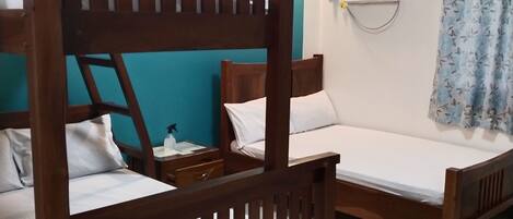 Um quarto com duas camas de solteiro de madeira, um ar condicionado branco na parede e uma cortina azul.