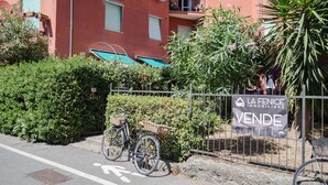 Um edifício vermelho com varandas, uma bicicleta e um aviso de 'La Fenice Immobiliare Vende'.