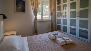 Quarto de hotel com cama, mesa de cabeceira, luminária, pintura e porta de vidro corrediça com painéis jateados.